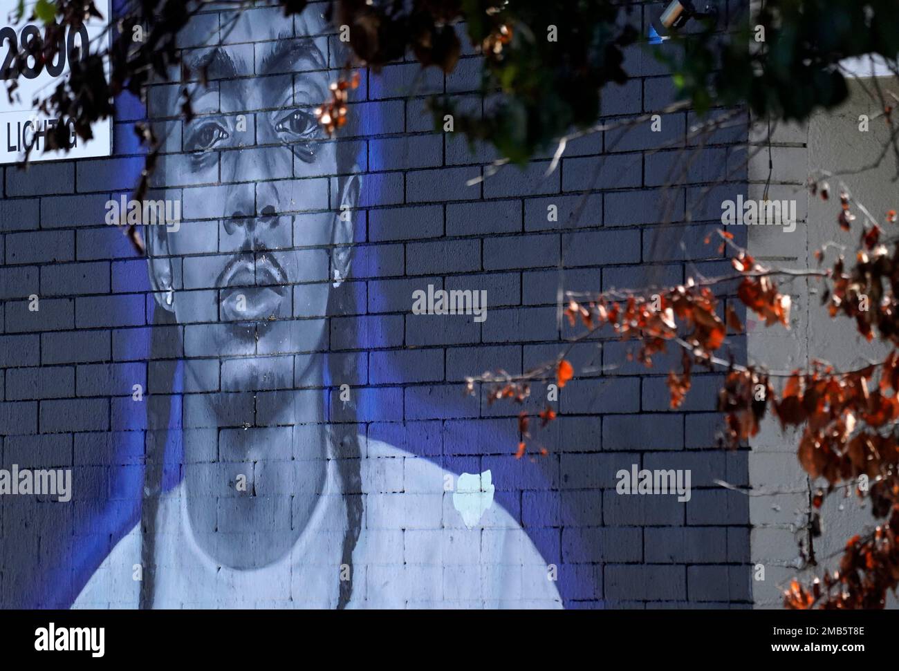 A street mural of the late rapper Nipsey Hussle is framed through tree ...