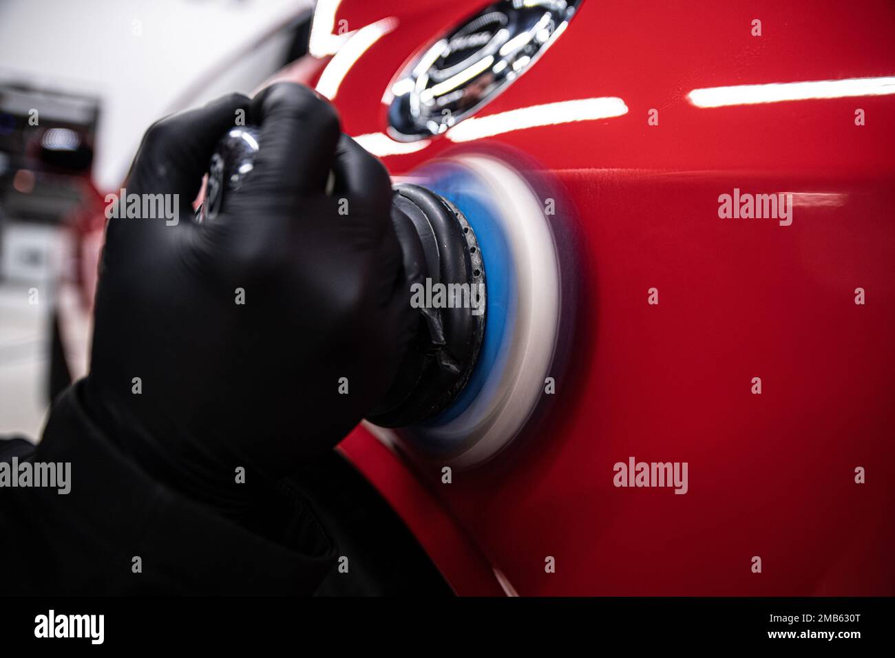 employee of a car detailing studio polishes the paintwork of a red car ...