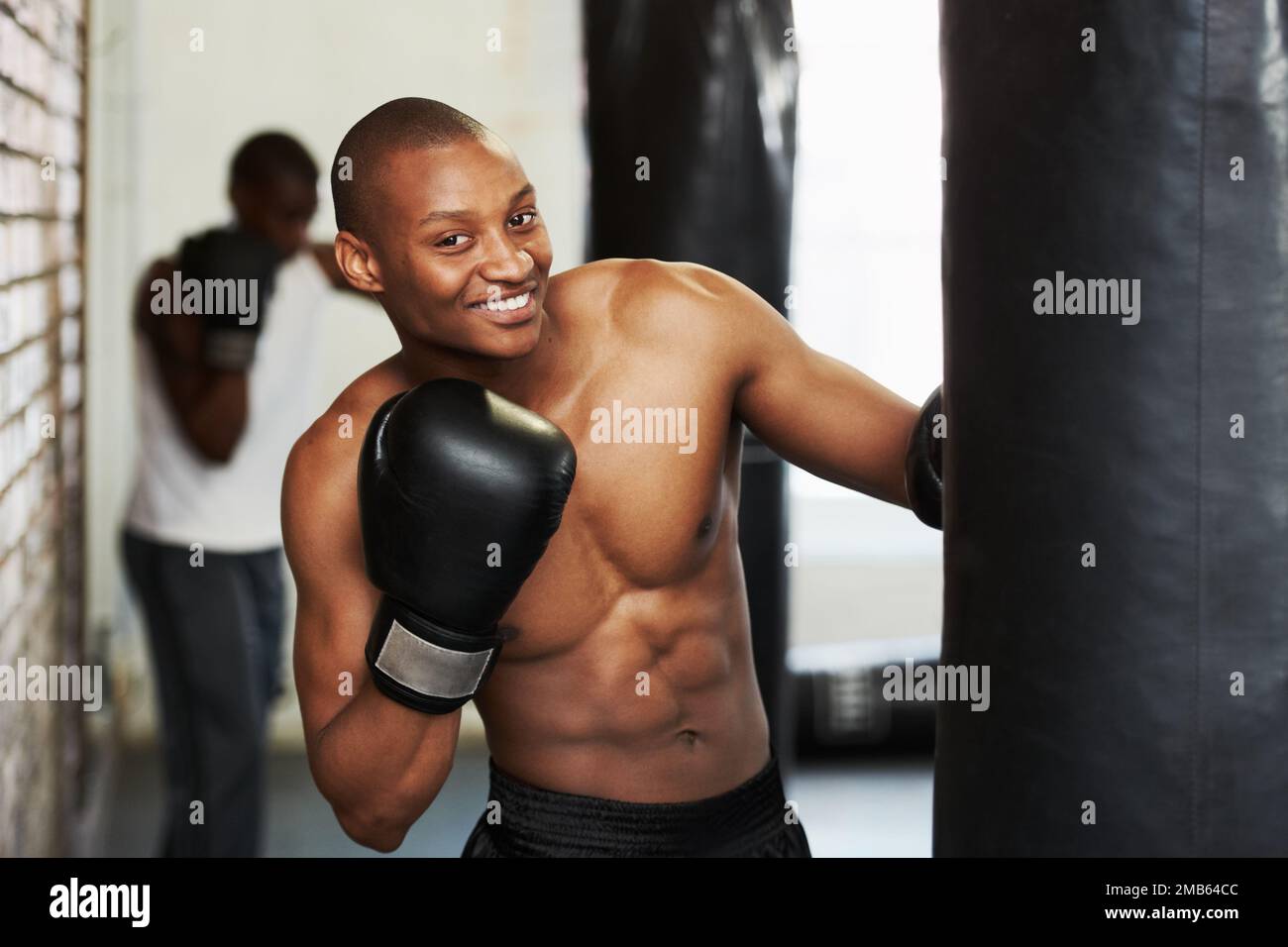 Enjoying the challenge. A smiling young boxer smacking a punching bag ...