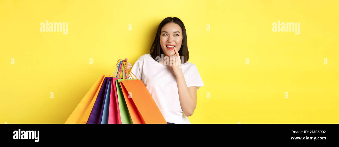 Pensive young woman smiling intrigued, showing shopping bags, thinking ...
