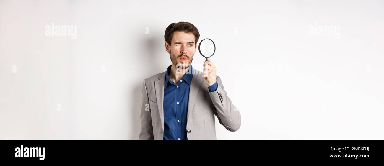 Handsome male model in suit looking through magnifying glass with ...