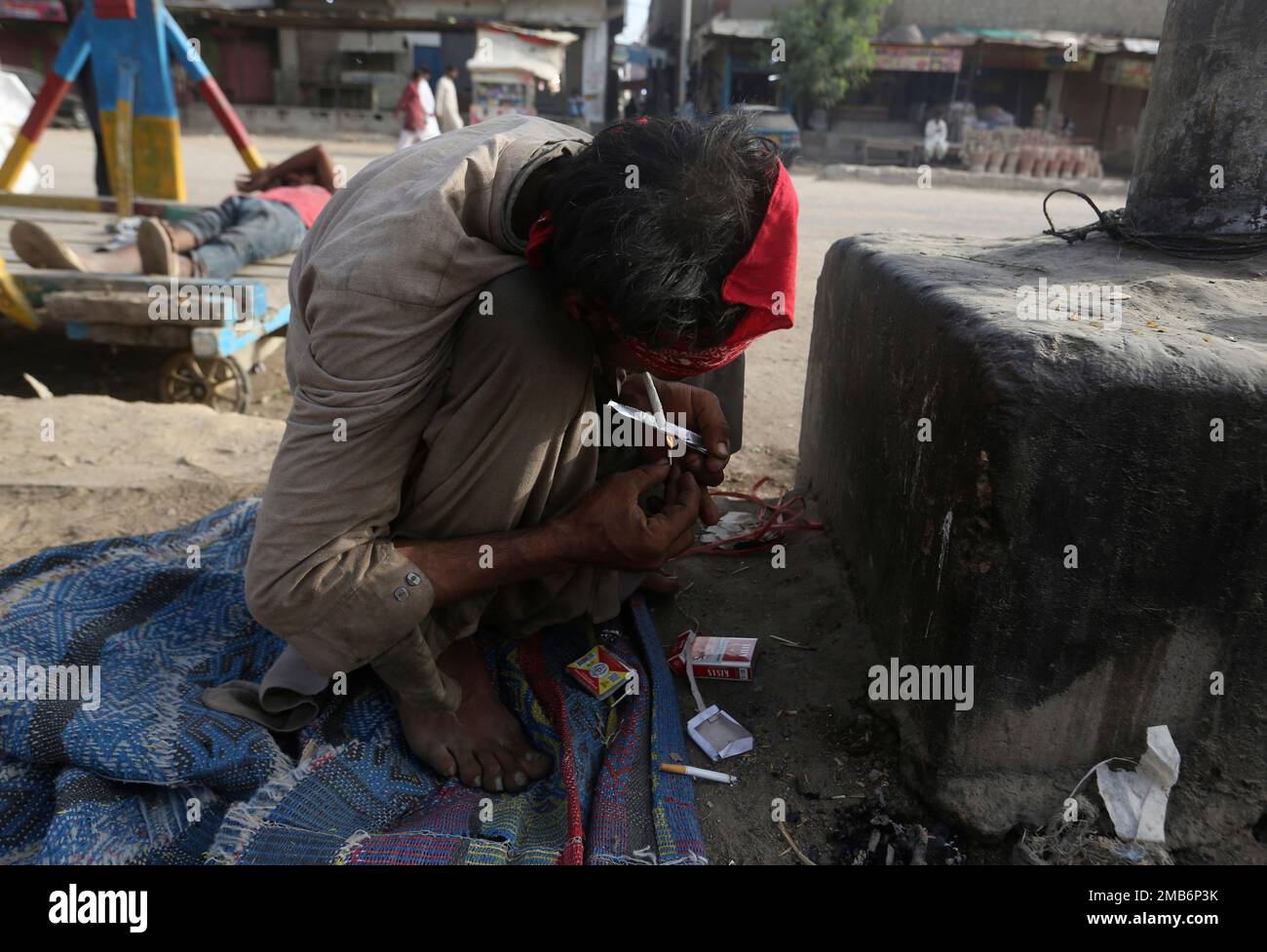 A Pakistani drug addict smokes heroin on a roadside in Karachi ...