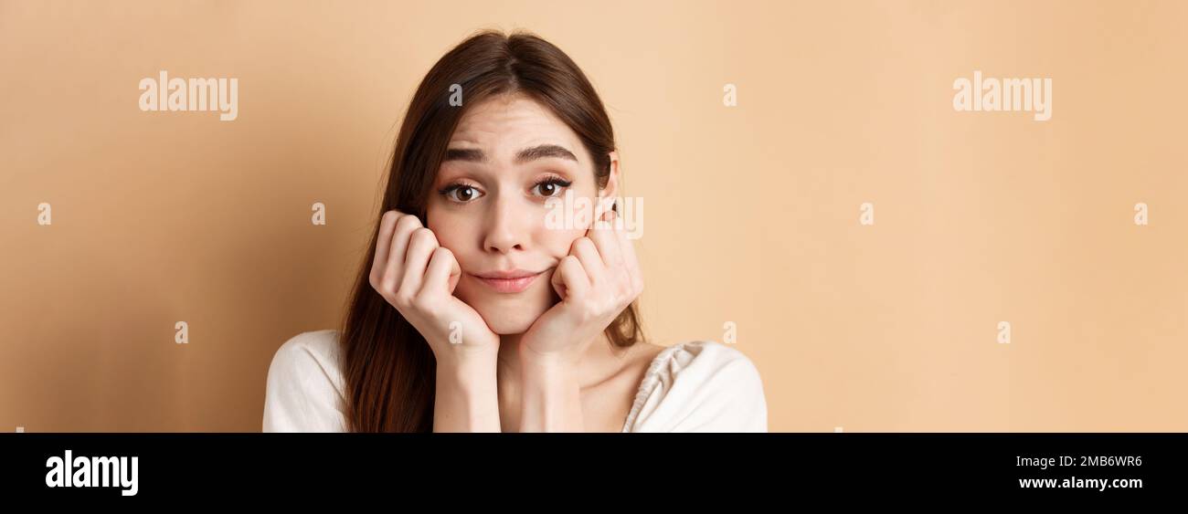 Close-up of cute and pretty girl lean face on hands, looking at camera ...