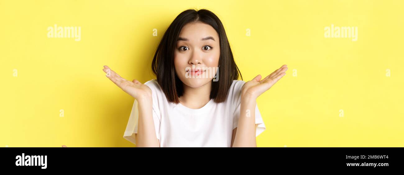 Silly mistake. Close up of cute asian girl saying sorry, shrugging ...