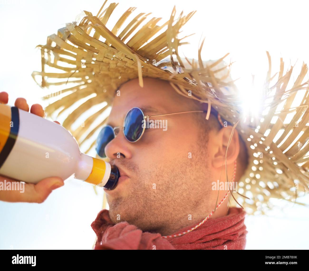 Taking a sip. a young man wearing a straw hat drinking out of a bottle ...