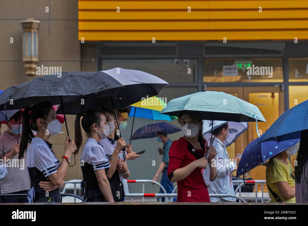Workers and residents wearing face masks line up in the rain for COVID ...