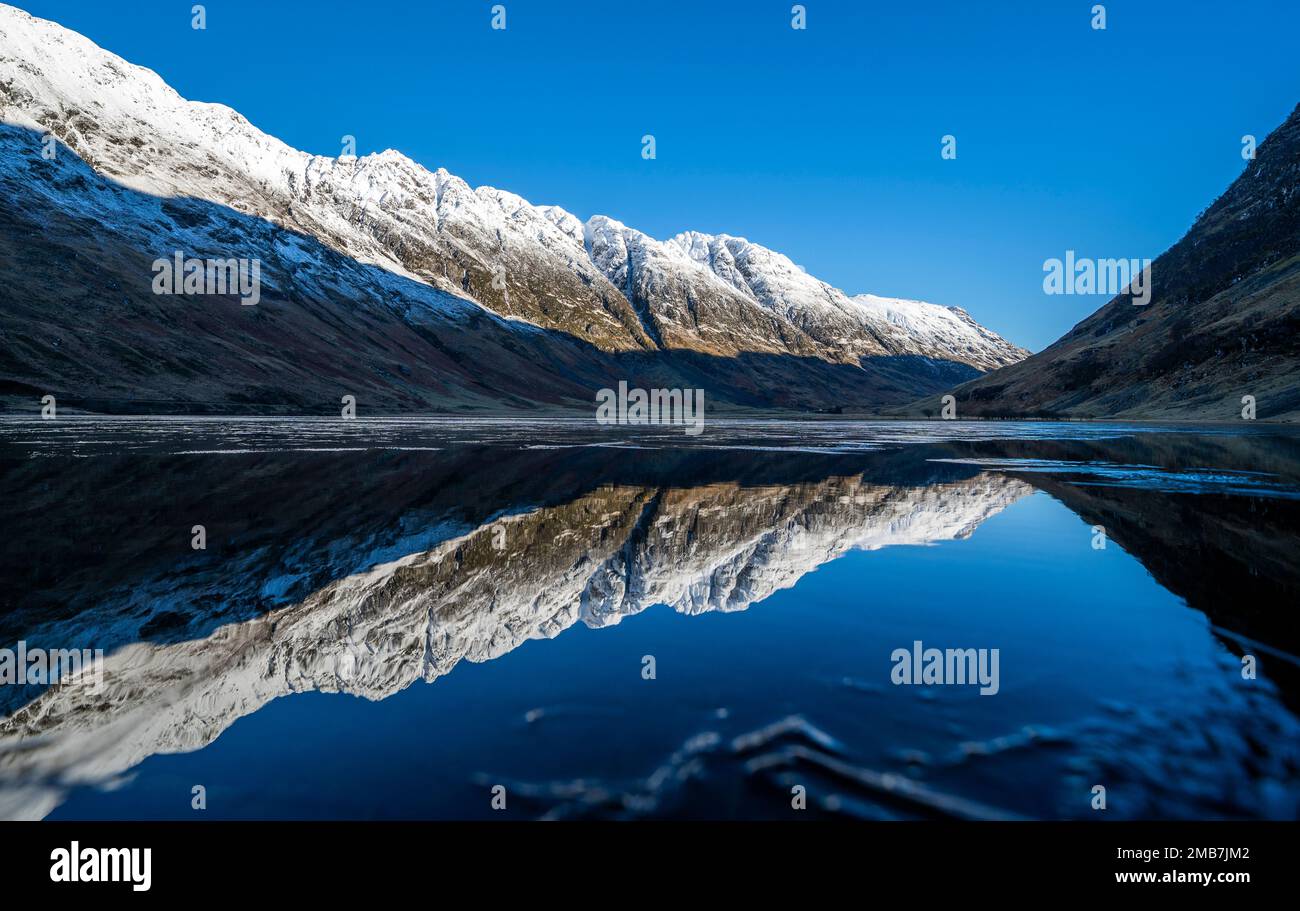 The snow covered peaks in Glencoe reflected in Loch Achtriochtan ...