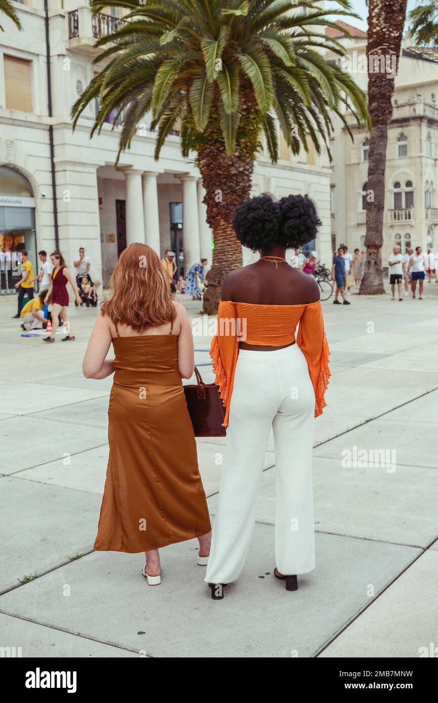 A back view of two stylish women posing at the city square on a summer ...