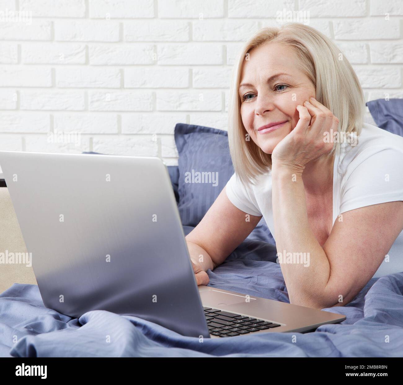 Smiling attractive woman lying on bed using laptop communicating online ...