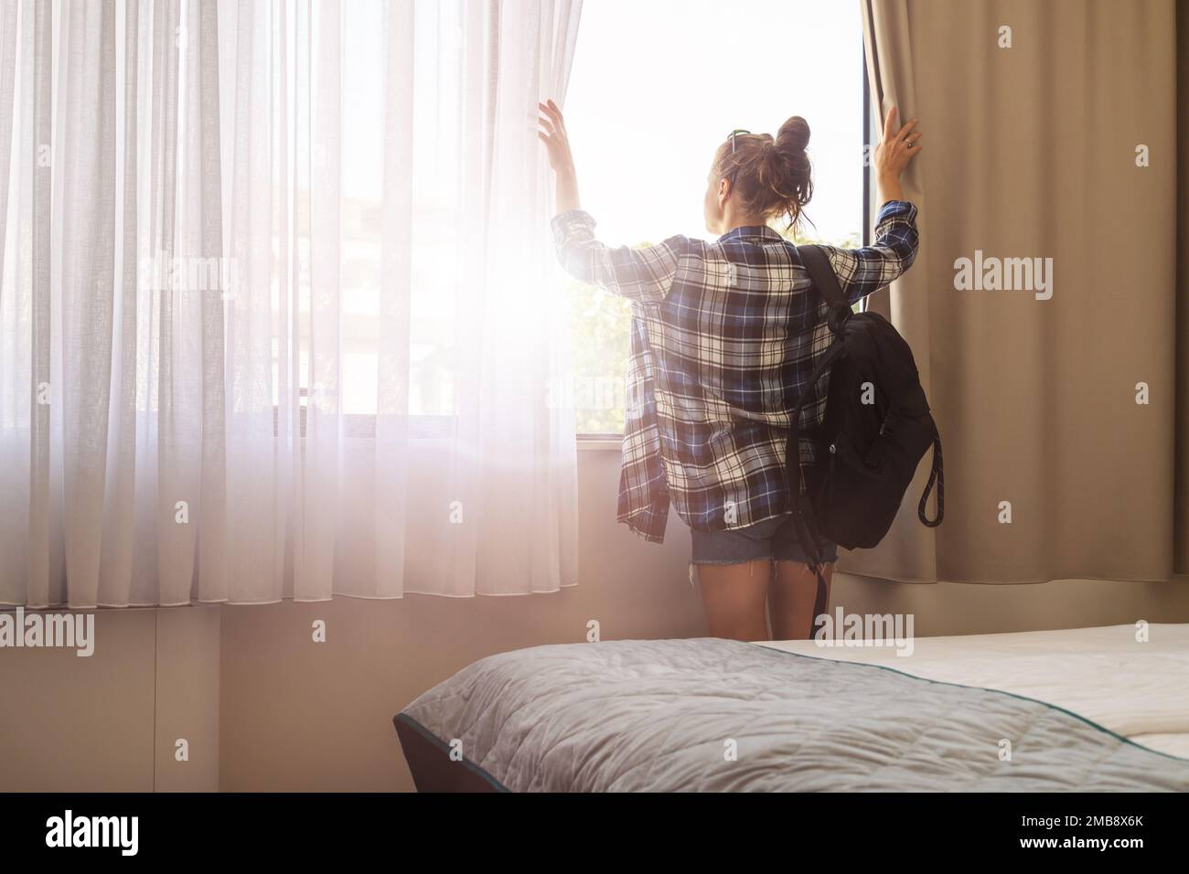 Woman tourist with backpack standing in hotel room pulling back ...