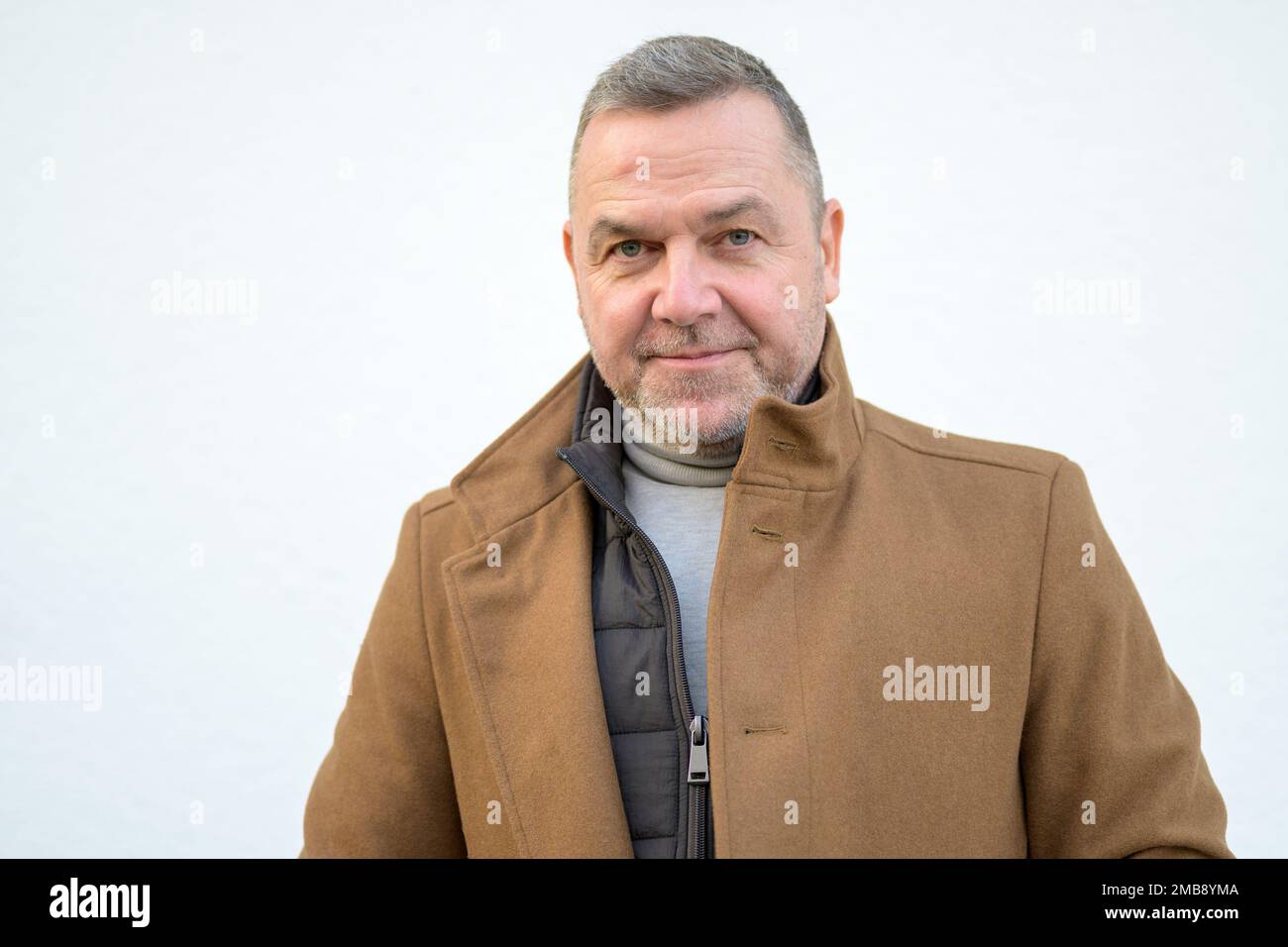 Portrait of a middle aged serious man in a brown coat against a neutral ...