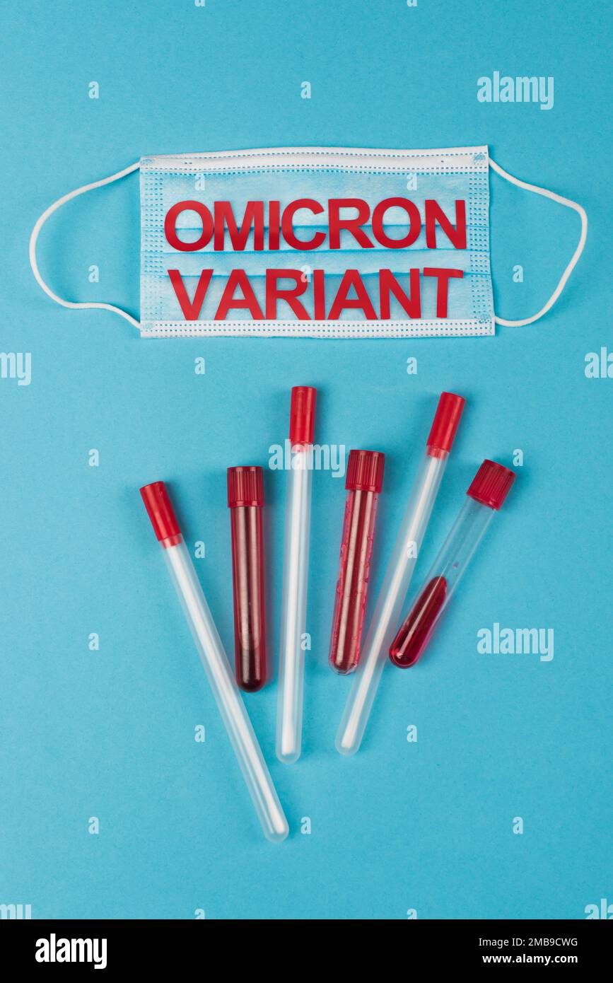 Top view of medical mask with omicron variant near test tubes and ...