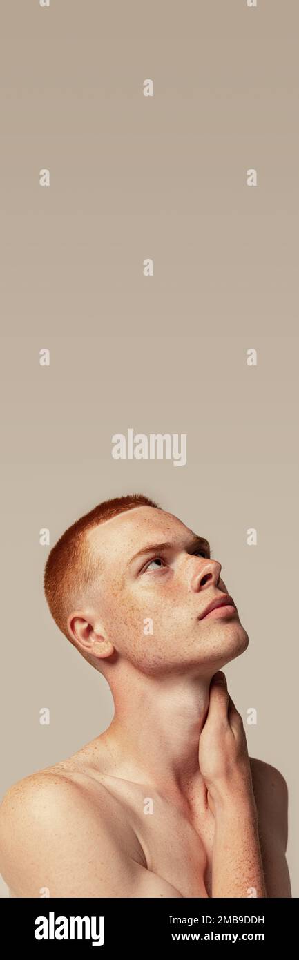 Handsome young red-haired man posing isolated over grey studio ...