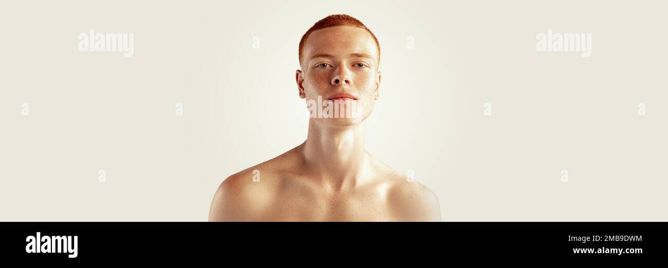 Handsome young red-haired man posing isolated over grey studio ...
