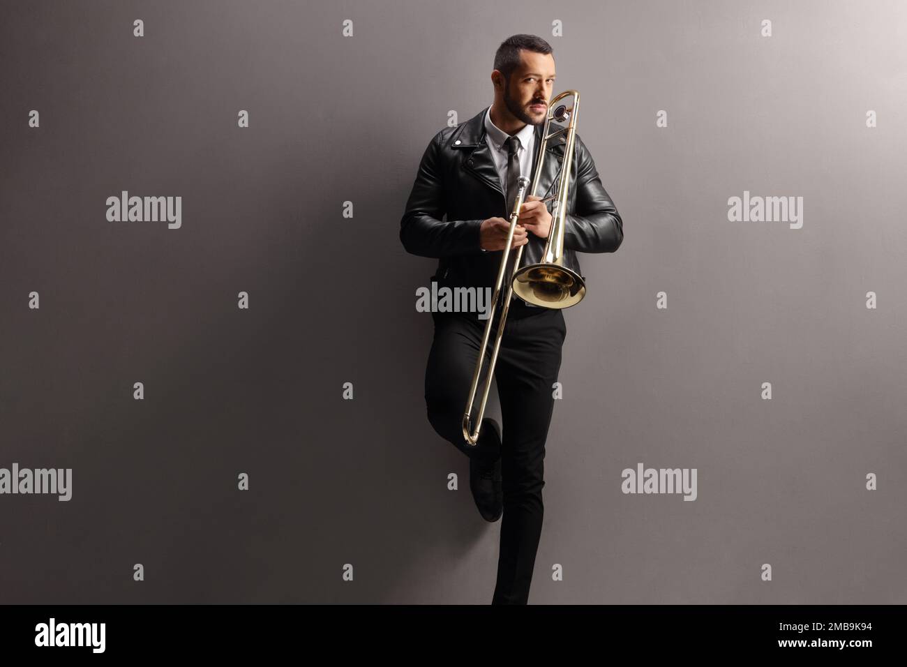 Young man with a trombone standing and leaning on a grey wall Stock ...