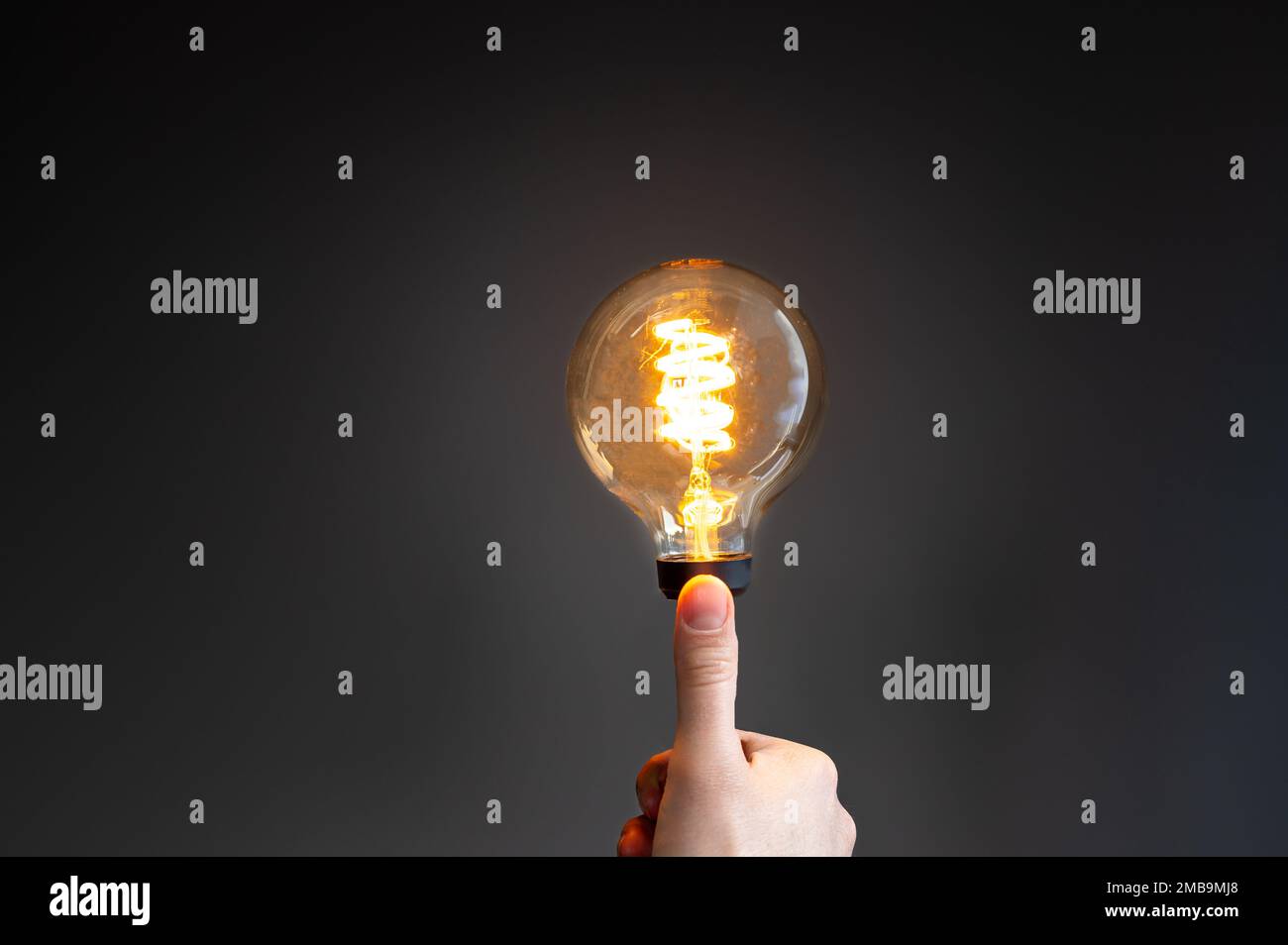 Symbol for saving energy. Hand holds a filament light-bulb where the ...