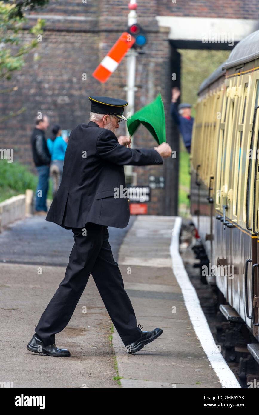 A steam train guard waves his green flag to the engine driver as a ...