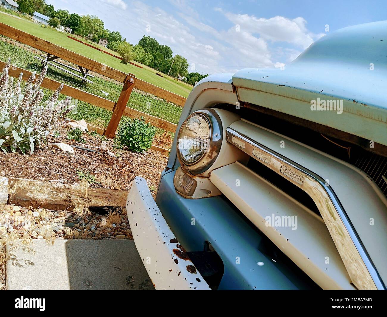 A closeup of Ford Fairlane blue car with cloudy sky and green field ...