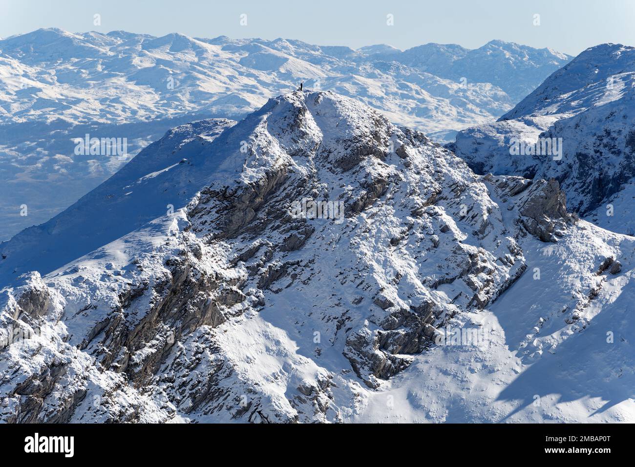 Solo hiker stands on the top of a mountain peak with snow. Vast winter ...