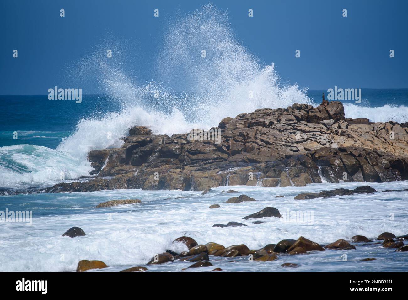 Strong waves breaking at a rocky shore against a clear bue sky Stock ...