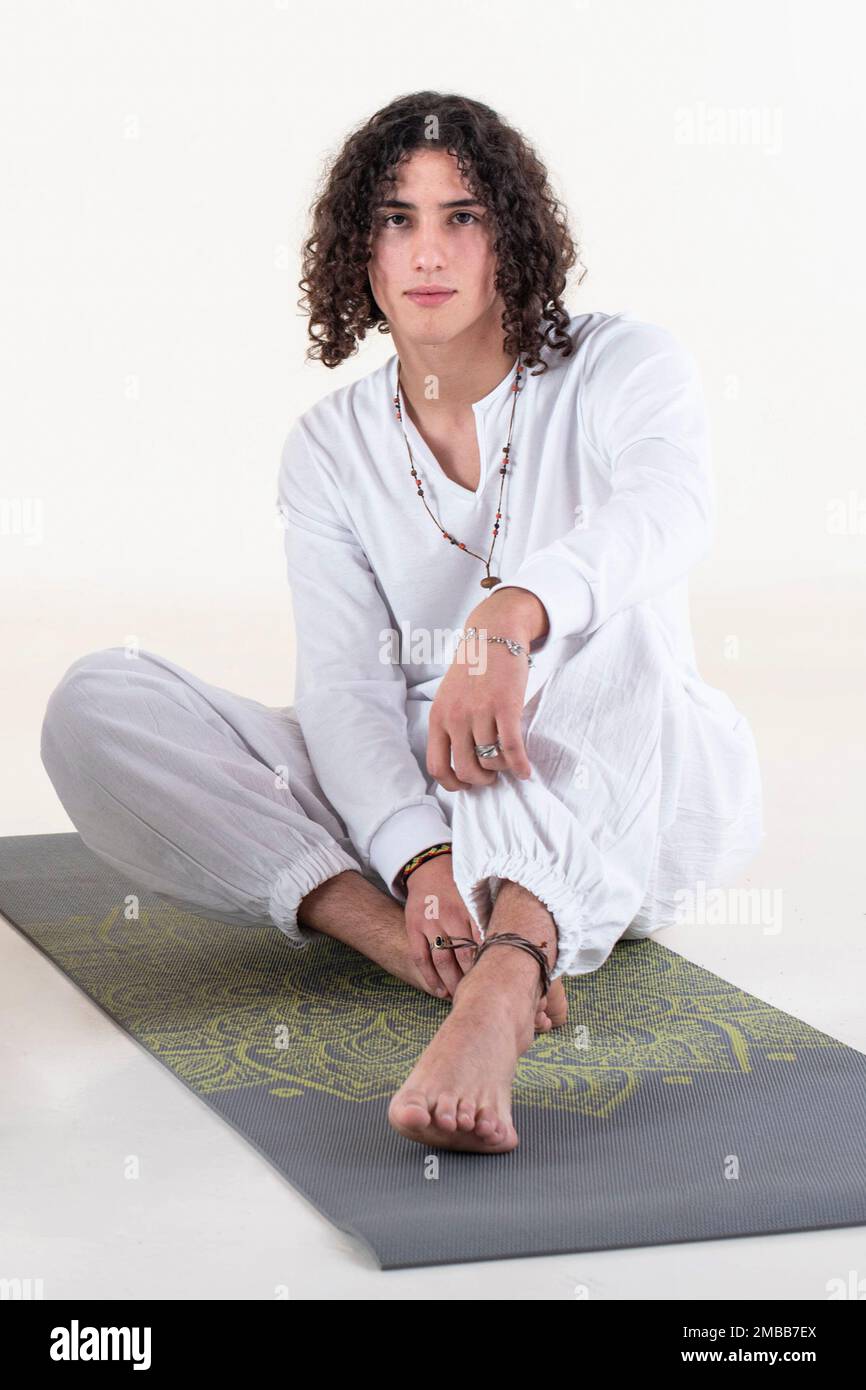 Young man sitting on a mat about to meditate while looking at camera ...