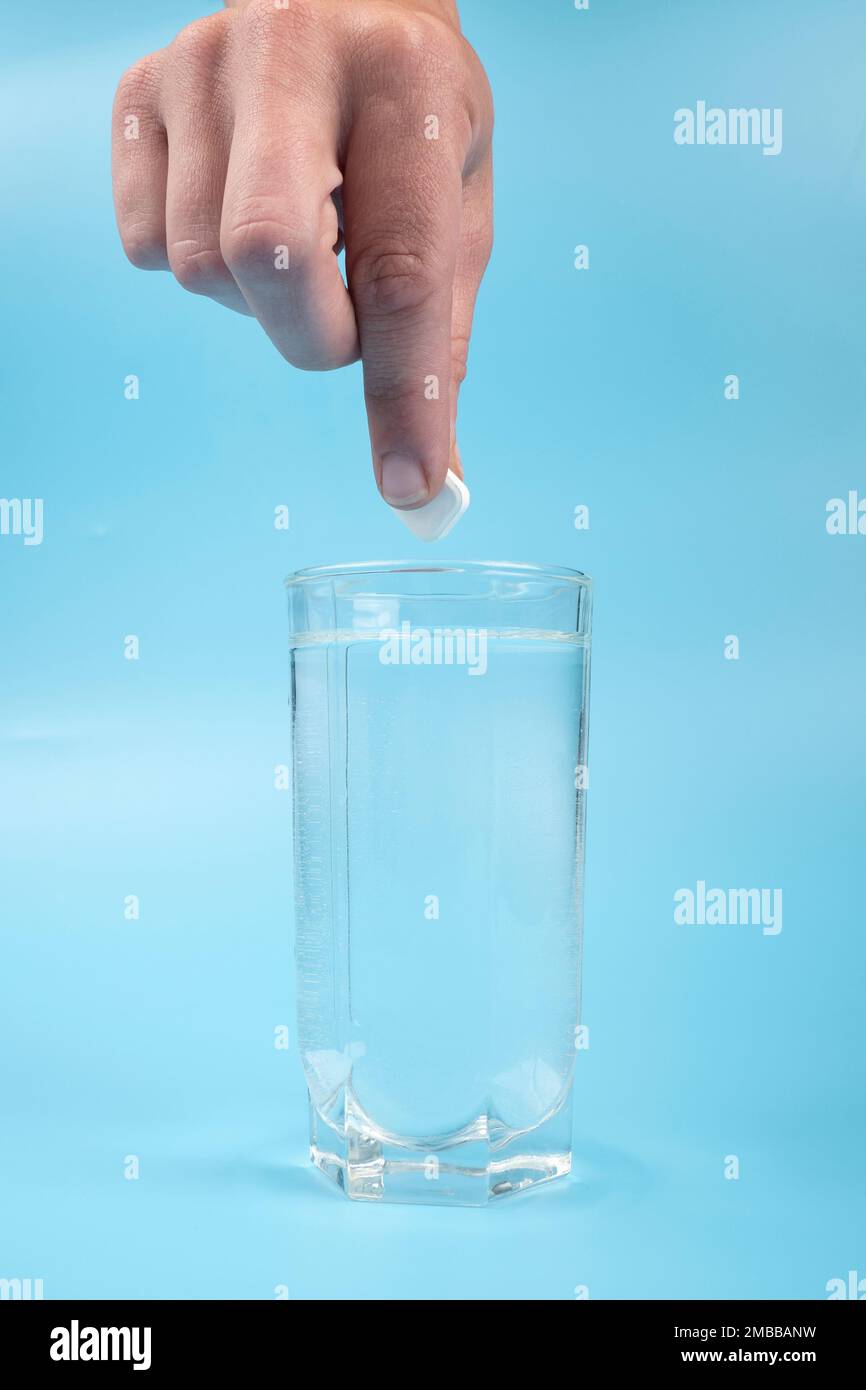 glass cup with water and a hand with a pill on blue background ...