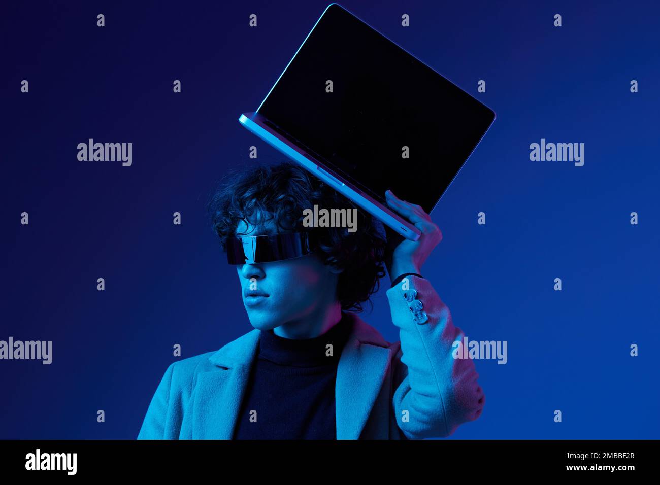 Portrait of a stylish male hacker with a laptop and futuristic glasses ...