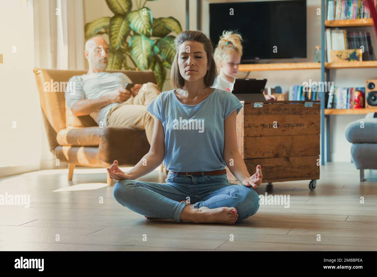 mother in lotus yoga pose tries to relax while husband and daughter ...