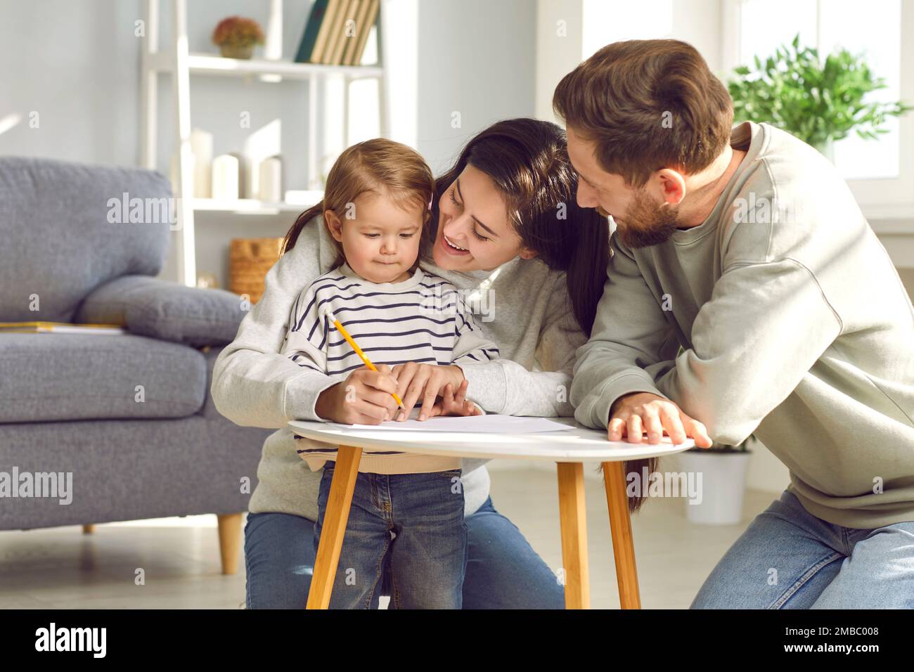 Caring mom and dad teach their little toddler daughter to draw with ...
