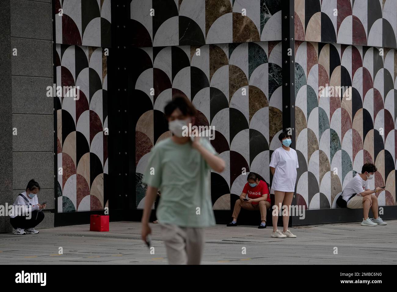 Residents wearing face masks wait outside a shopping mall after ...