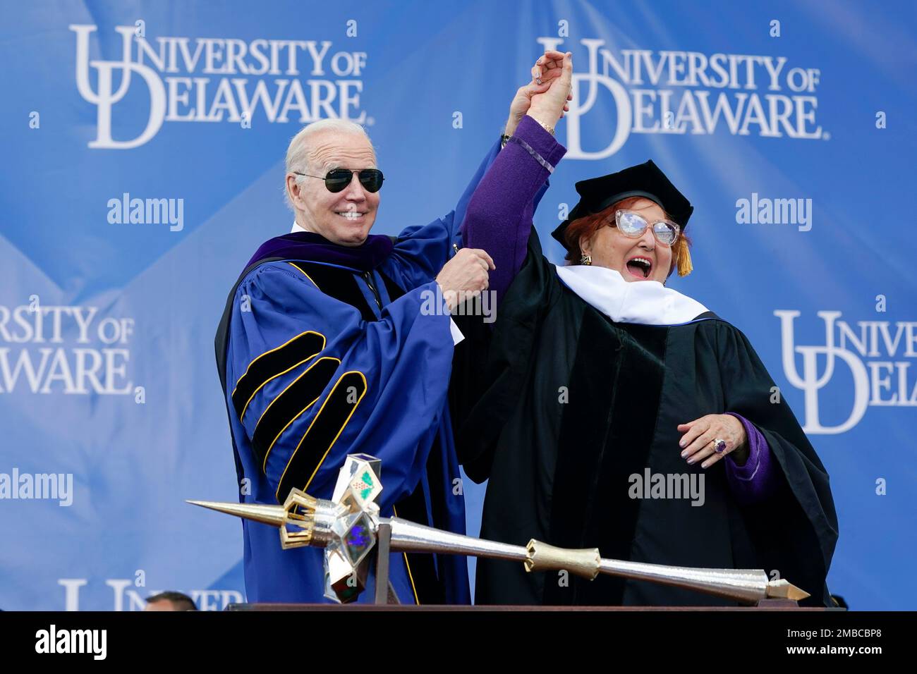 President Joe Biden holds up the hand of honorary degree recipient ...