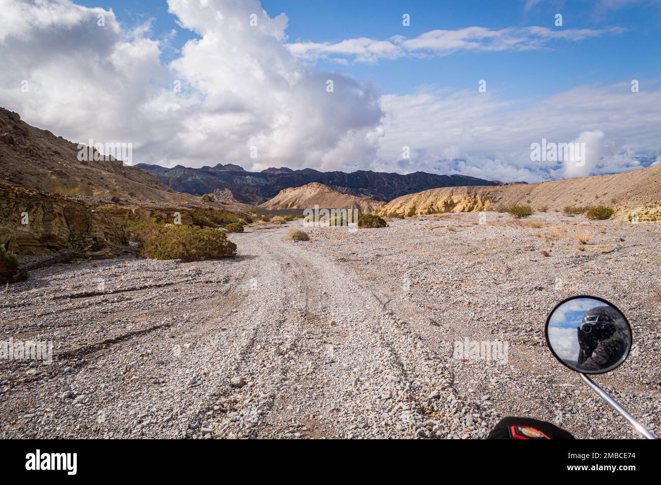 A man's face is reflected in a motorcycle mirror as he rides down a ...
