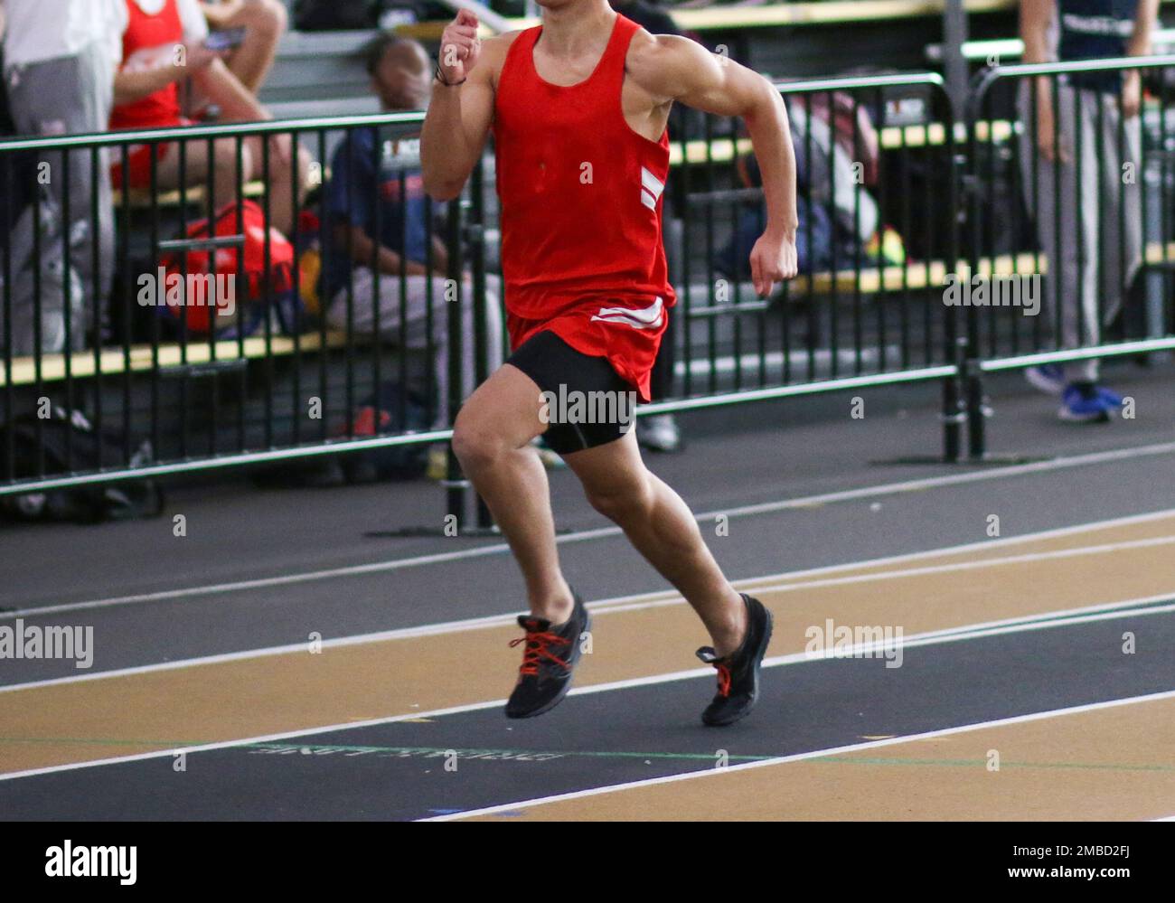 A male high school runner sprinting on an indoor track during a track ...