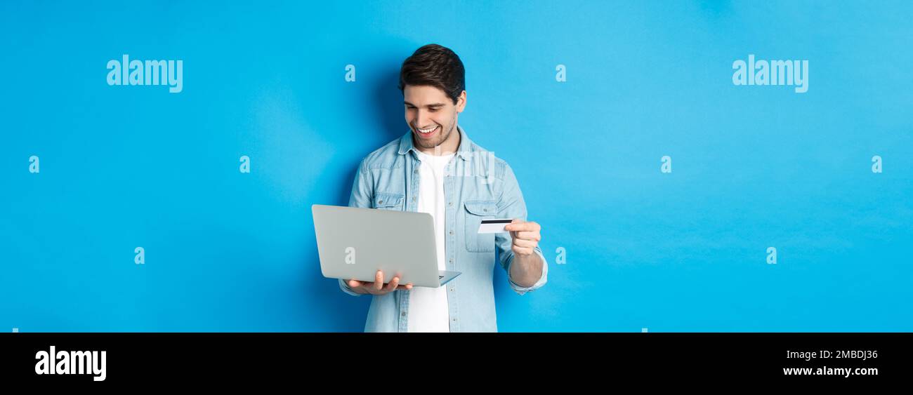 Young smiling man buying in internet, holding credit card and paying ...