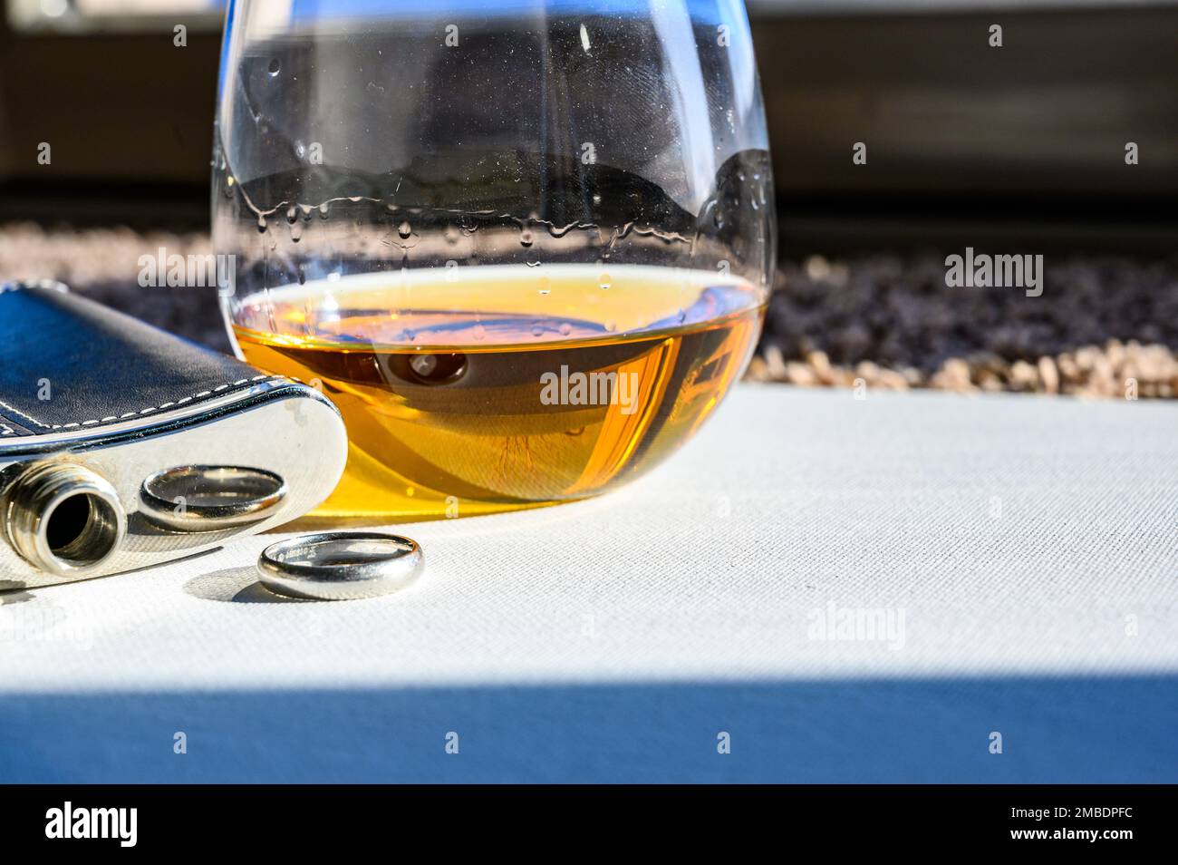Black and silver whiskey flask next to a glass of amber colored liquid ...