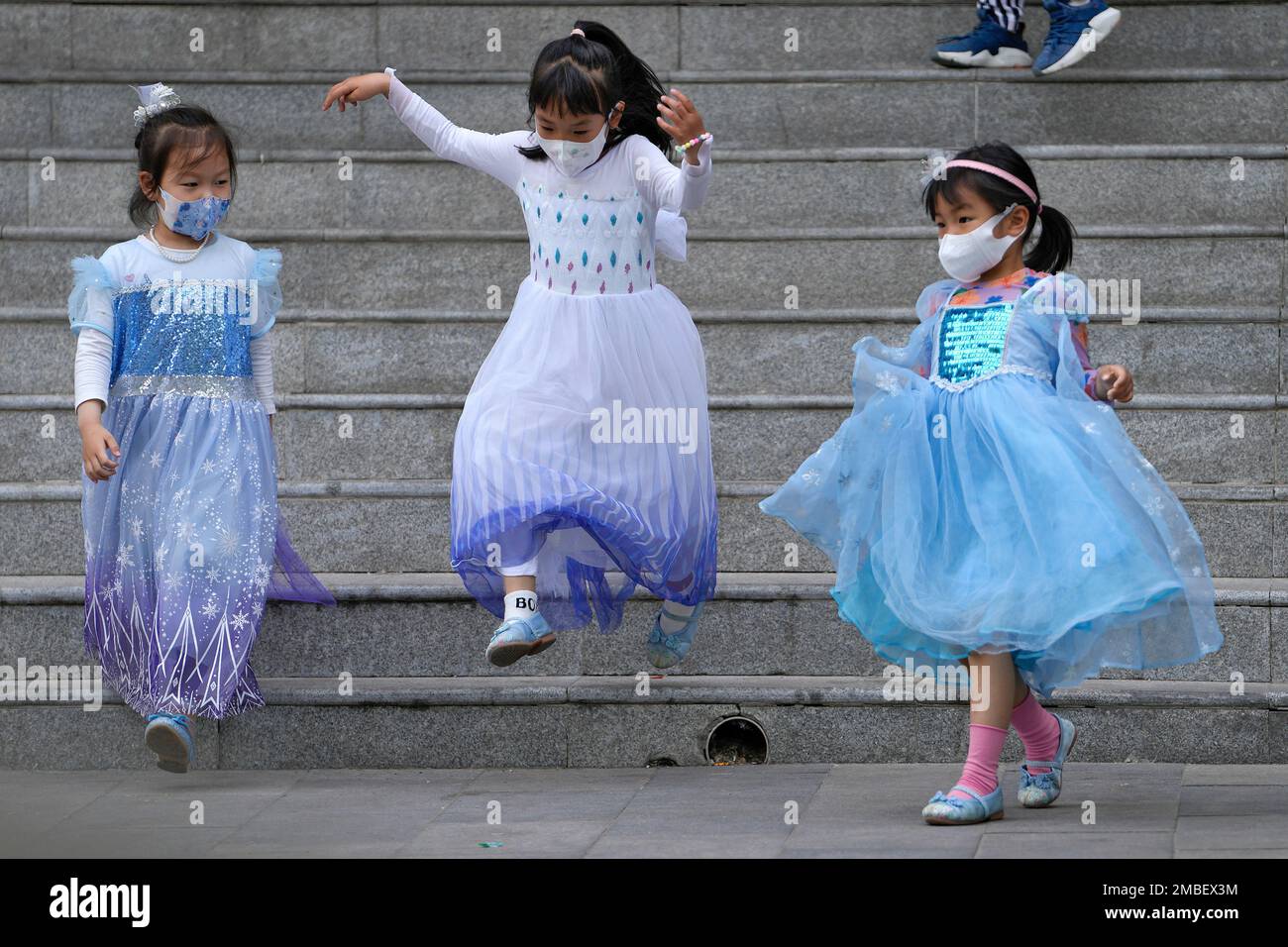 Children wearing princess dresses and face masks play on a staircases ...