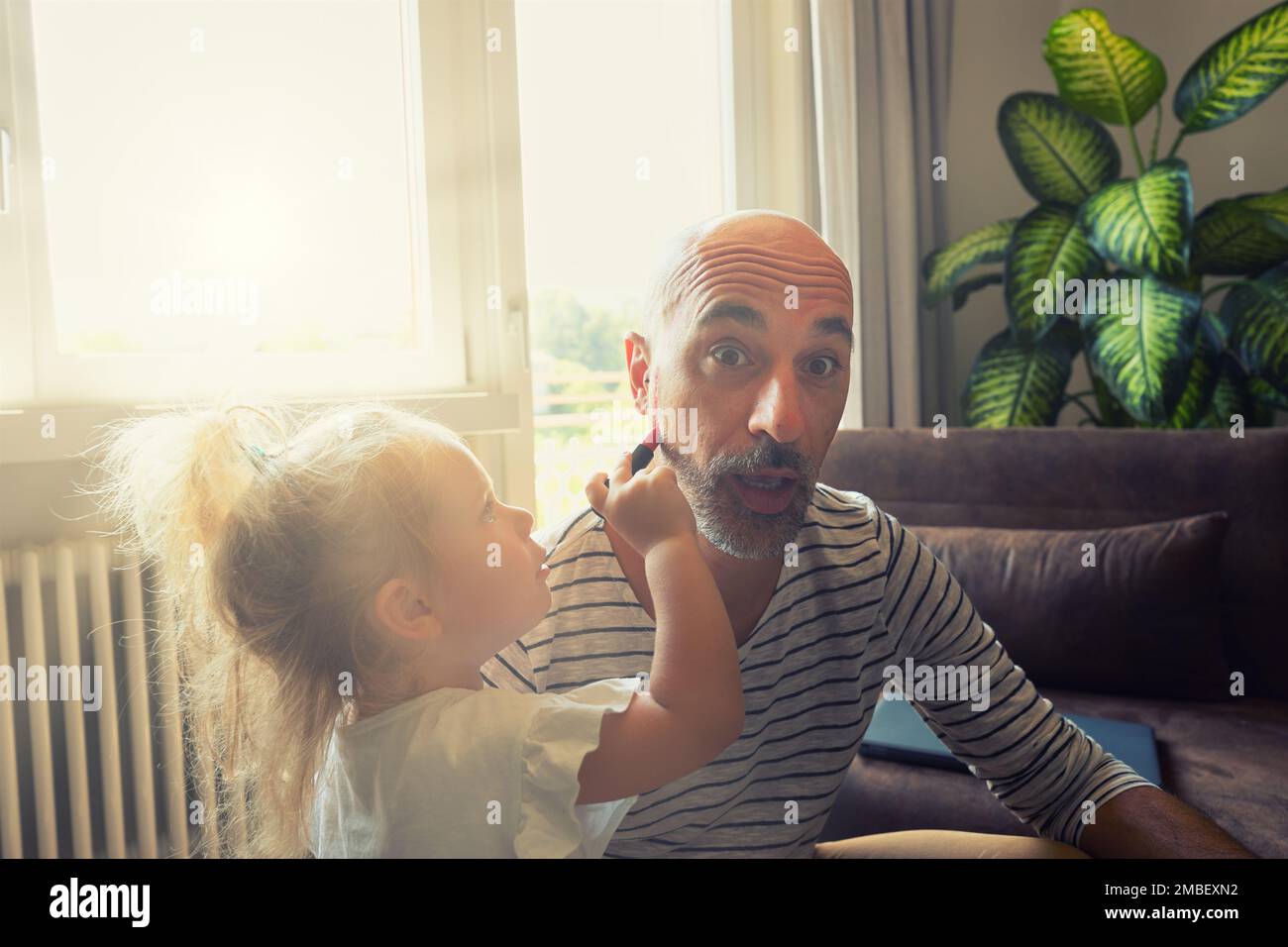 little girl artistically applies lipstick to the side of her daddy's ...
