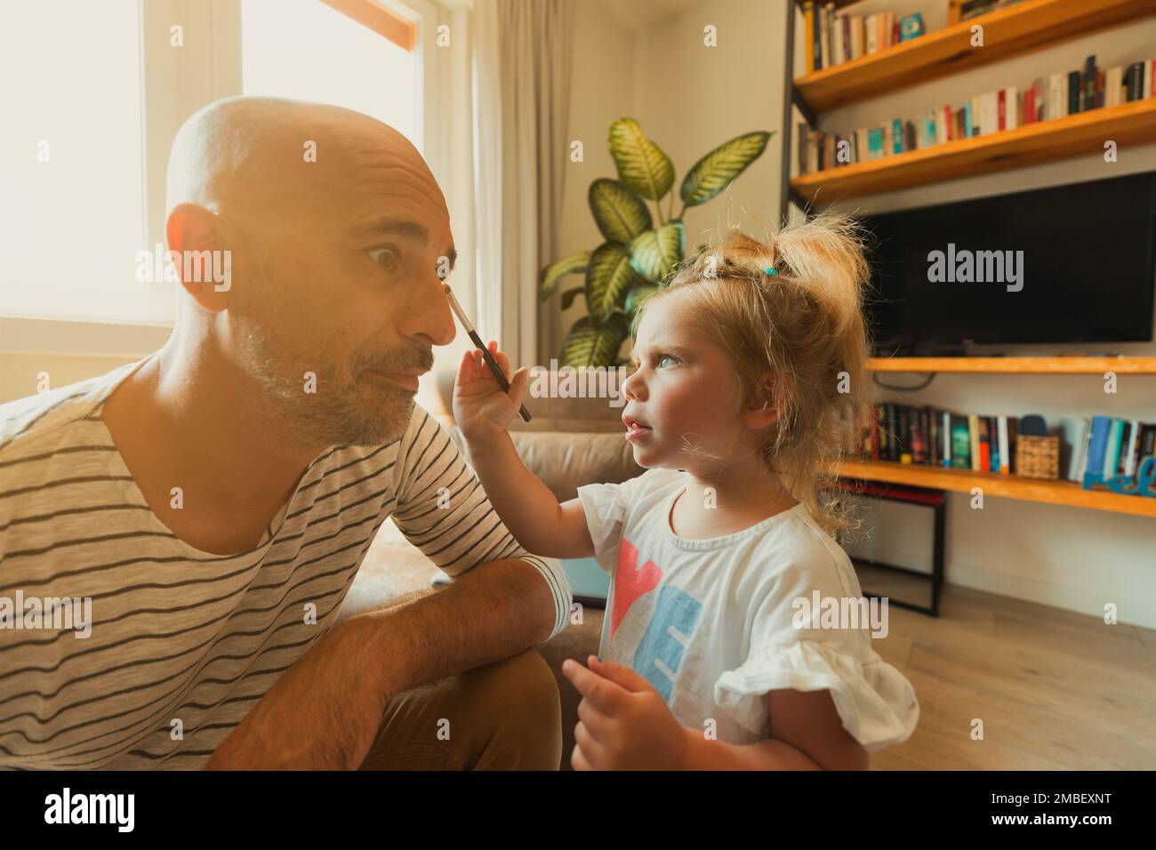 Little girl seriously busy putting make-up on her daddy, who makes a ...