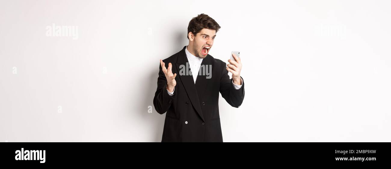 Portrait of angry businessman in black suit yelling at mobile phone ...