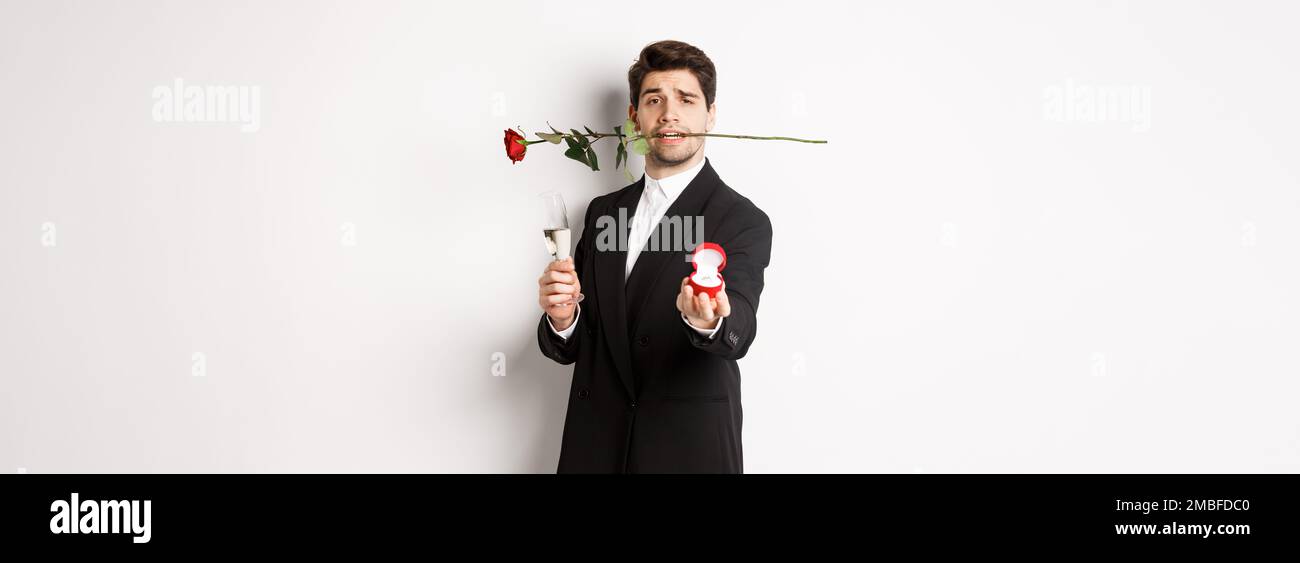 Romantic young man in suit making a proposal, holding rose in teeth and ...