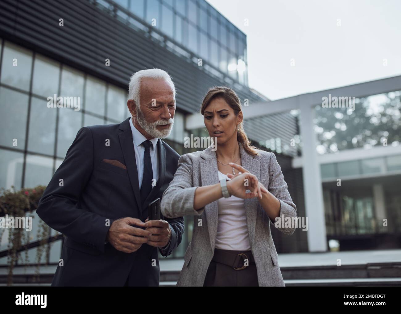 Senior businessman and young woman talking in hurry in front of office ...