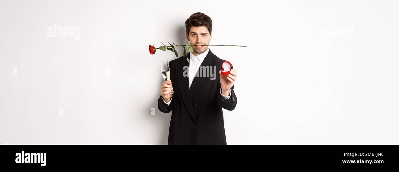 Passionate young man in suit making a proposal, holding rose in teeth ...