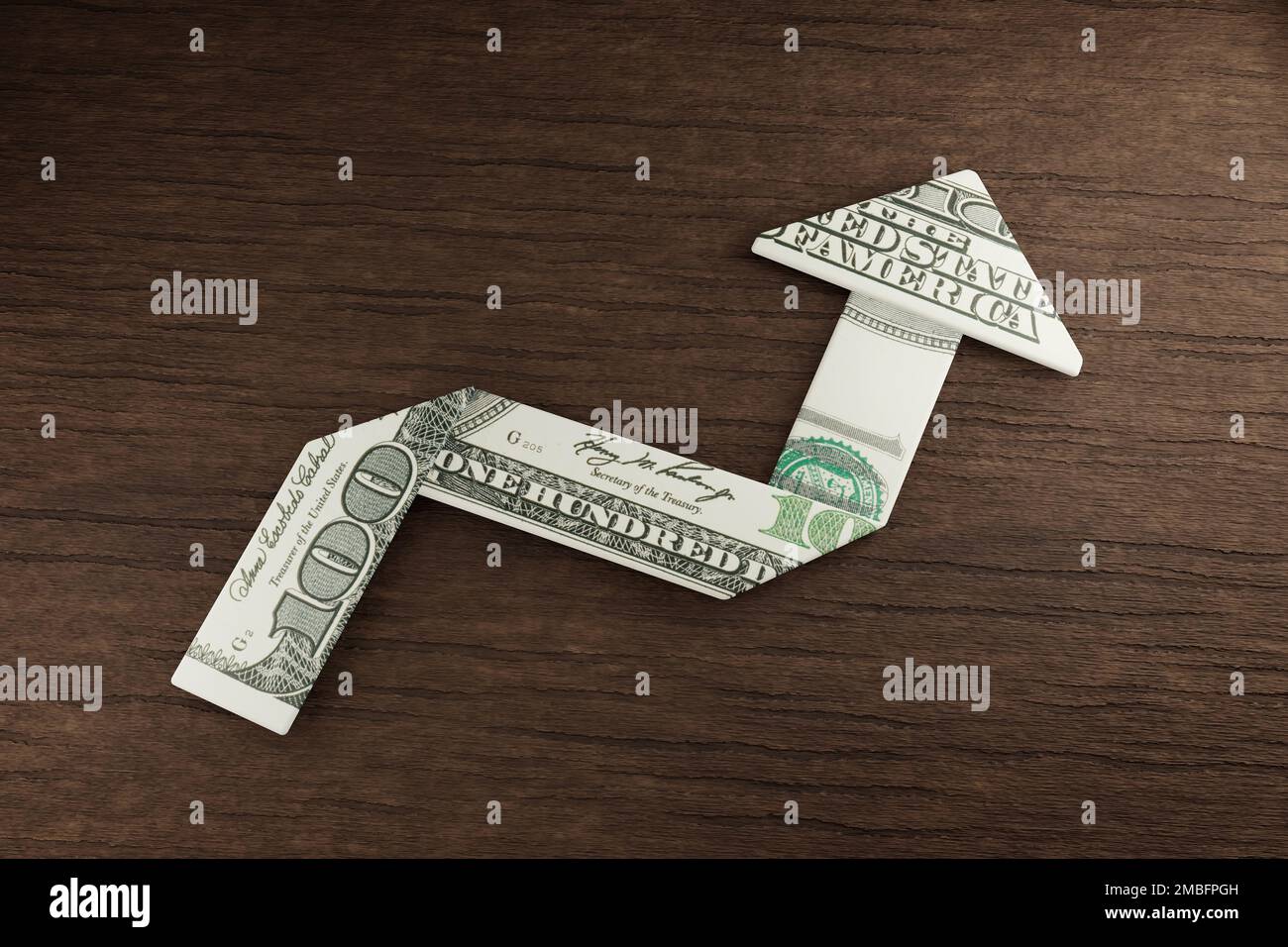 US 100 dollar bill folded into an up arrow on wooden table ...
