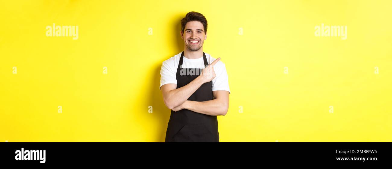 Happy barista pointing finger left and smiling, wearing black apron ...
