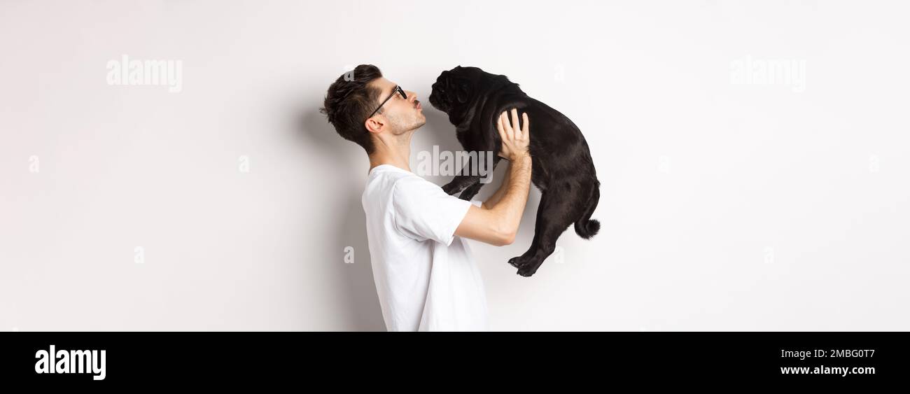 Profile of handsome young man kissing small cute dog face. Hipster guy ...