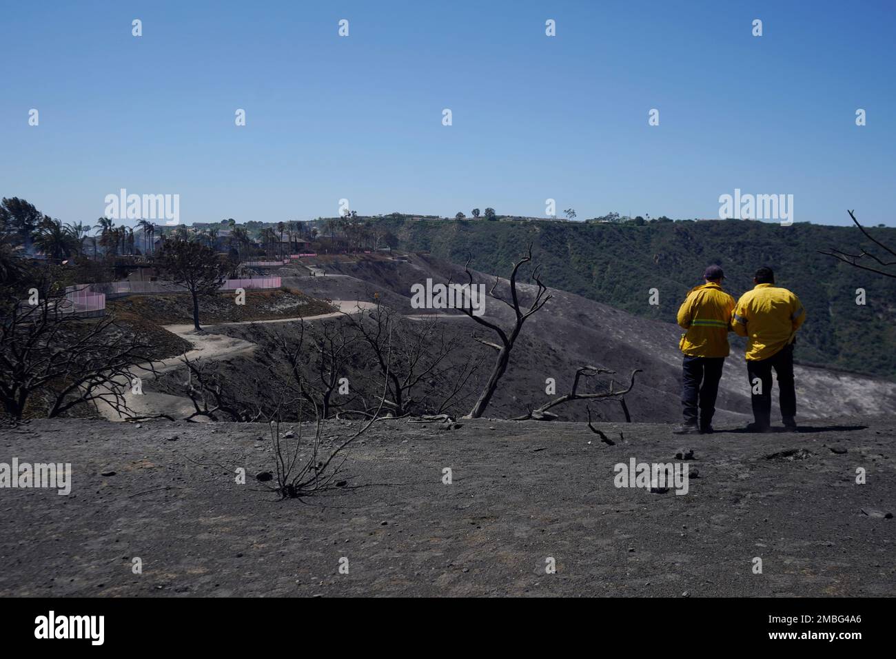 Firefighters stand on a ridge overlooking a fire-ravaged wilderness ...