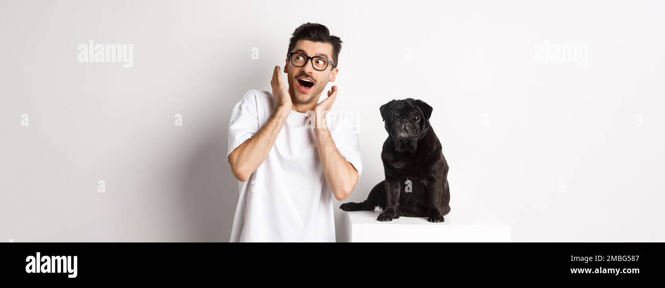 Amazed young man standing with cute black puppy, staring at upper right ...
