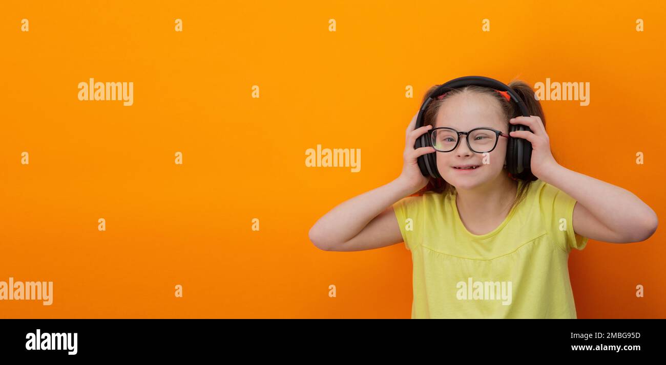 Girl with Down syndrome listens to music. Orange background. Banner Stock Photo - Alamy