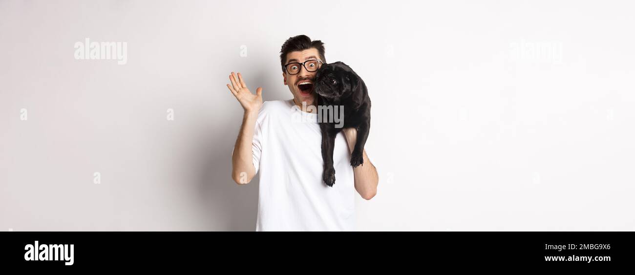 Handsome young man in glasses holding his black pug and waving hand ...
