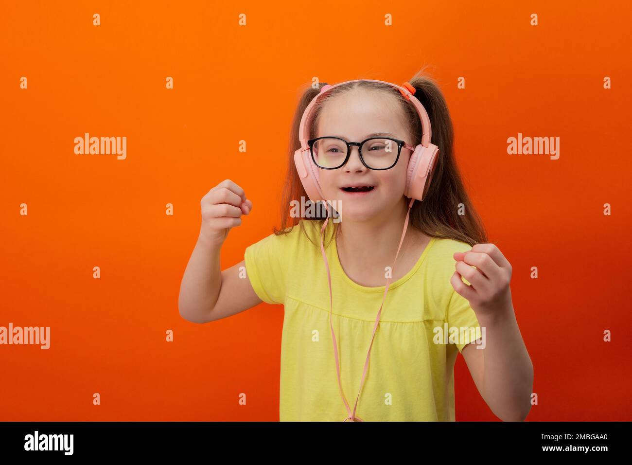 Girl with Down syndrome listens to music. Orange background. Banner Stock Photo - Alamy